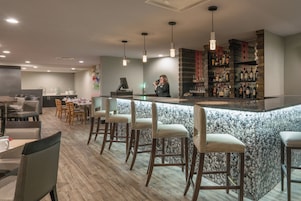 Uma área de bar com balcão, banquetas e diversas garrafas.