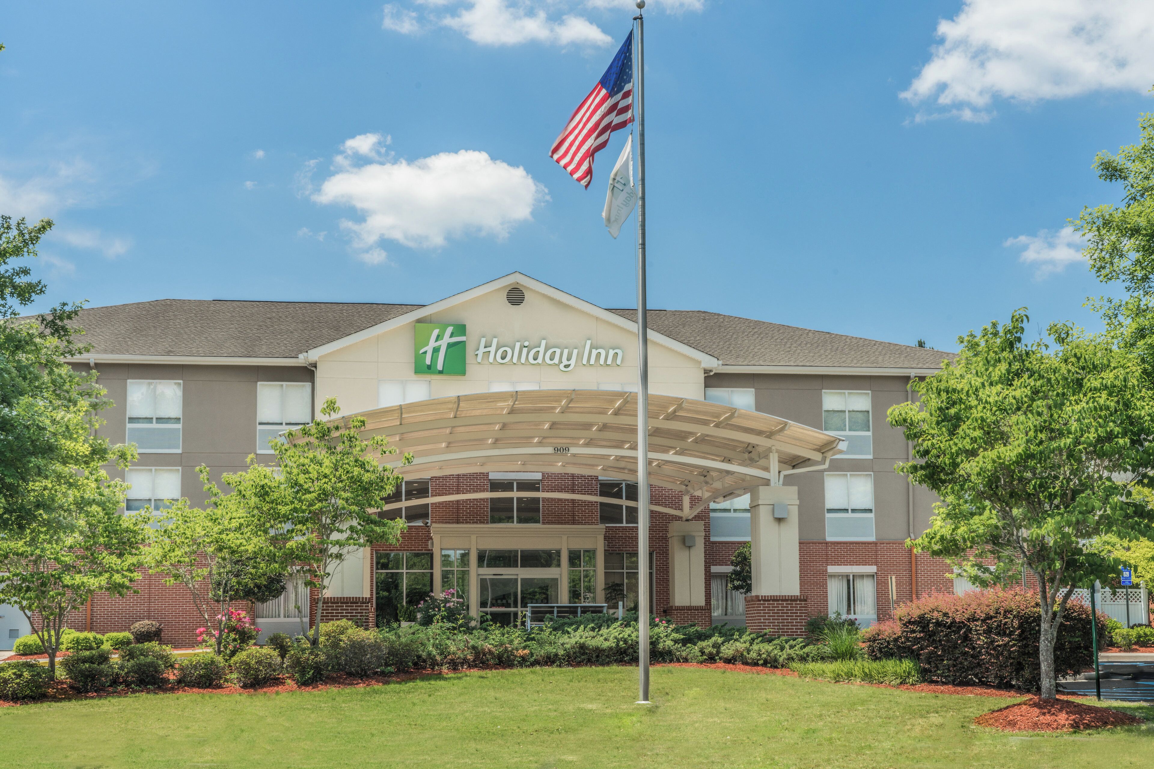 Um hotel Holiday Inn com entrada coberta, bandeira americana e jardins bem cuidados.