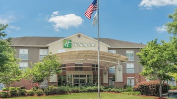 Um hotel Holiday Inn com entrada coberta, bandeira americana e jardins bem cuidados.