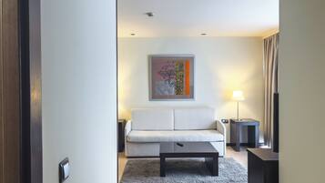 Uma sala de estar moderna com um sofá branco, uma mesa de centro preta, um tapete cinza, uma obra de arte emoldurada na parede e um abajur sobre uma mesinha lateral.