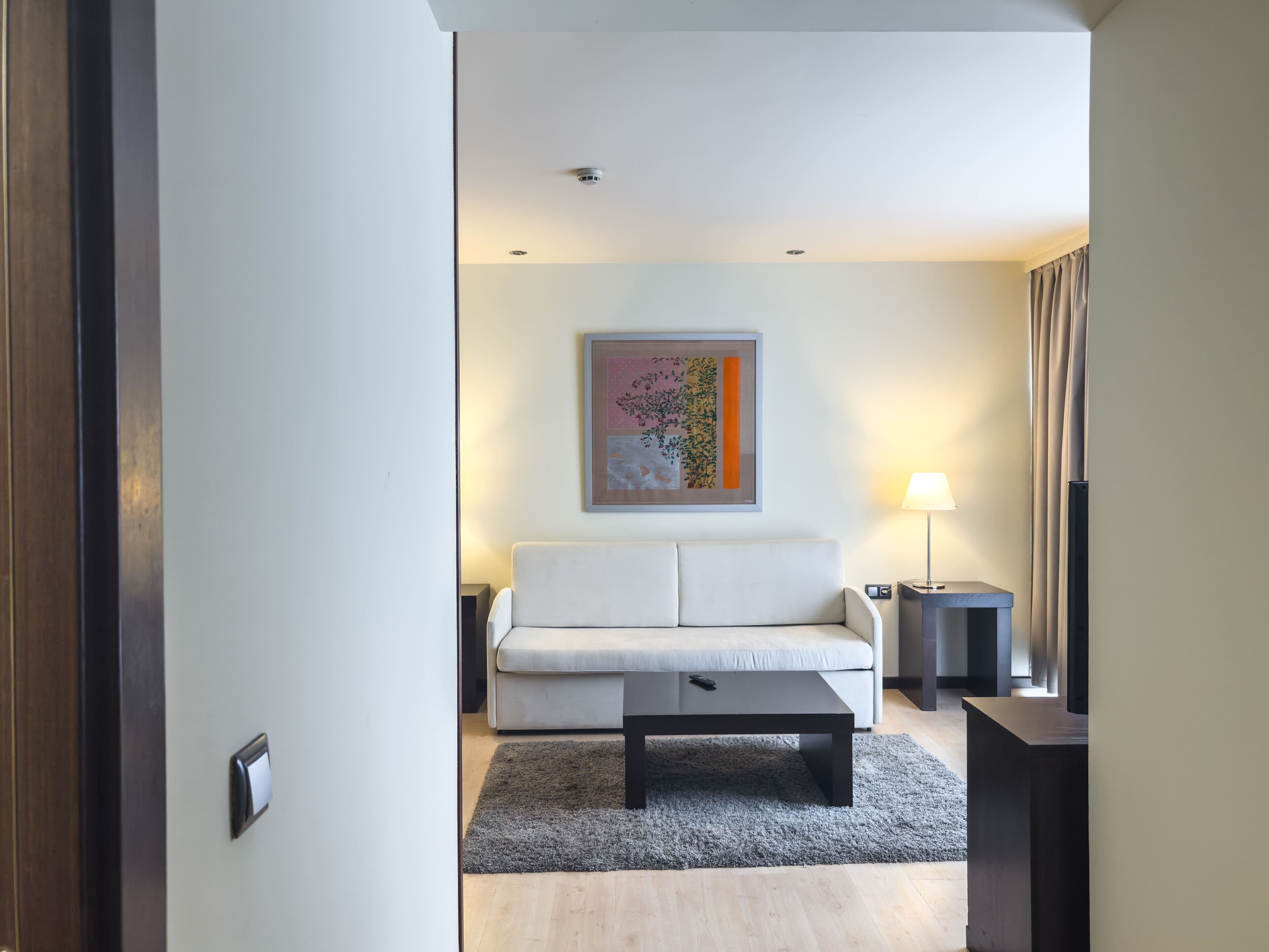 Uma sala de estar moderna com um sofá branco, uma mesa de centro e uma obra de arte emoldurada na parede.