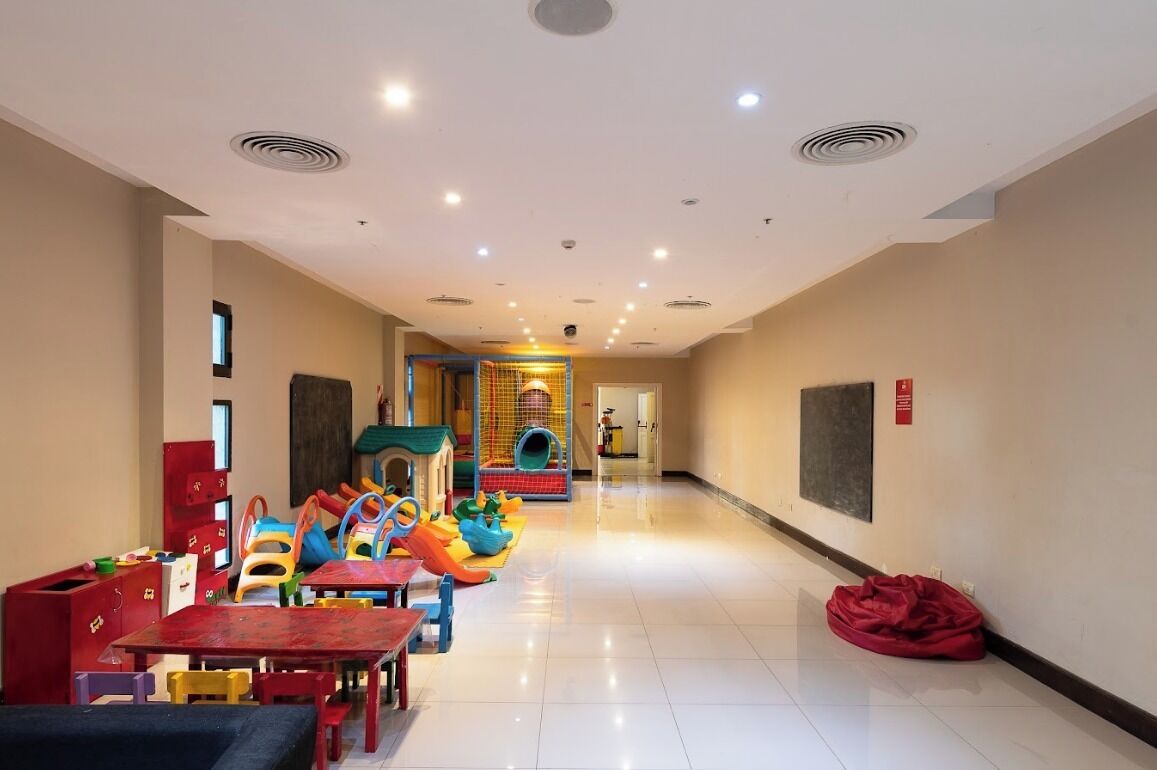 Espaço infantil com mesas, cadeiras e brinquedos.
