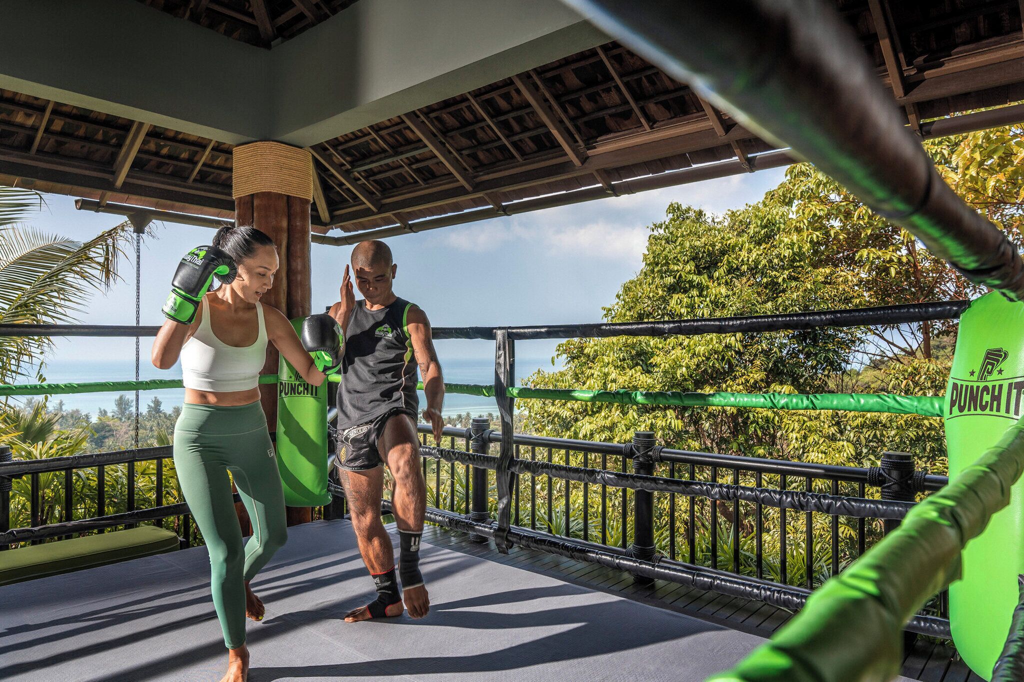 Espaço de treino de boxe com teto de madeira e vista para o mar.