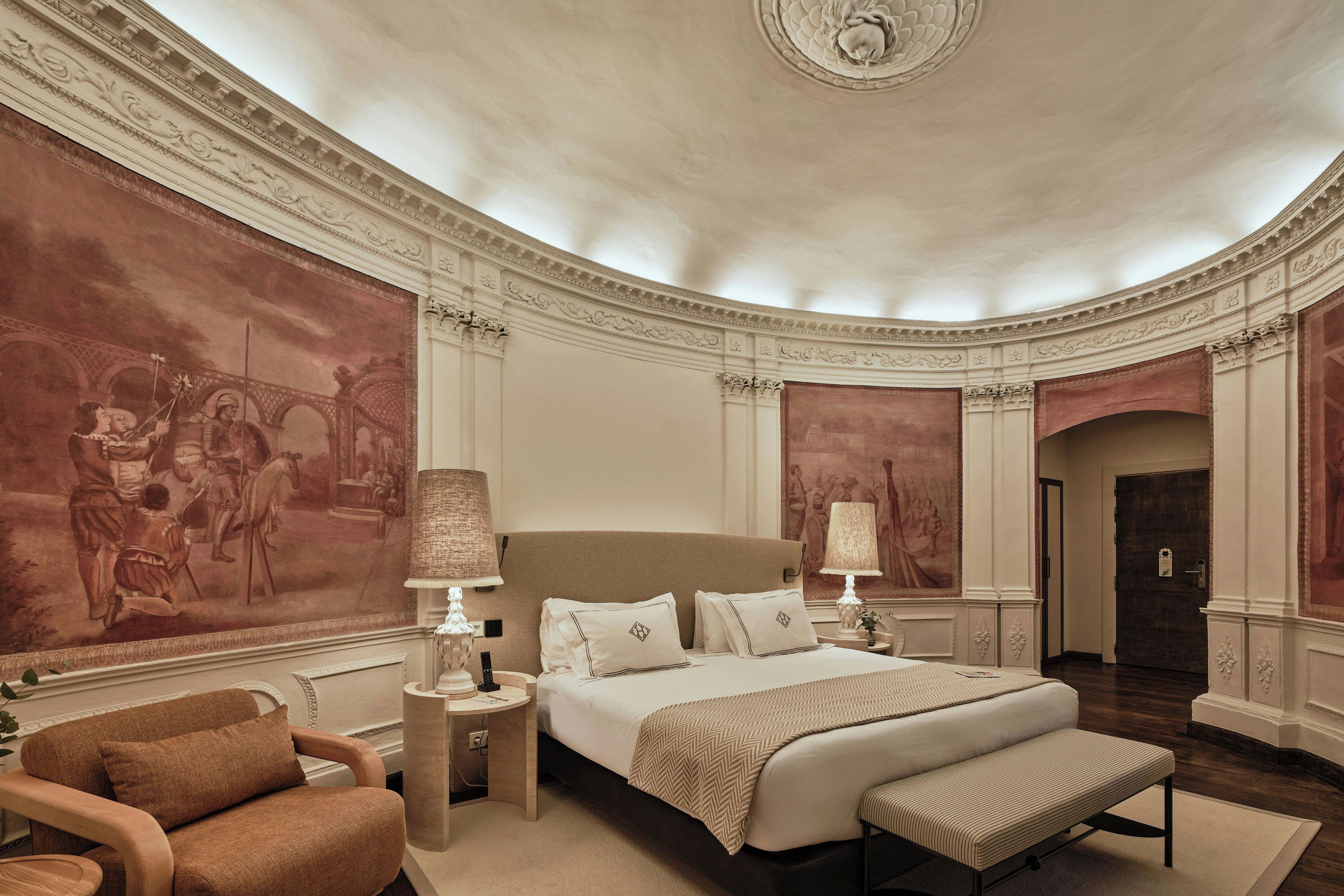 Um quarto luxuoso com uma cama grande, um espaço de estar com uma poltrona e um quadro na parede.