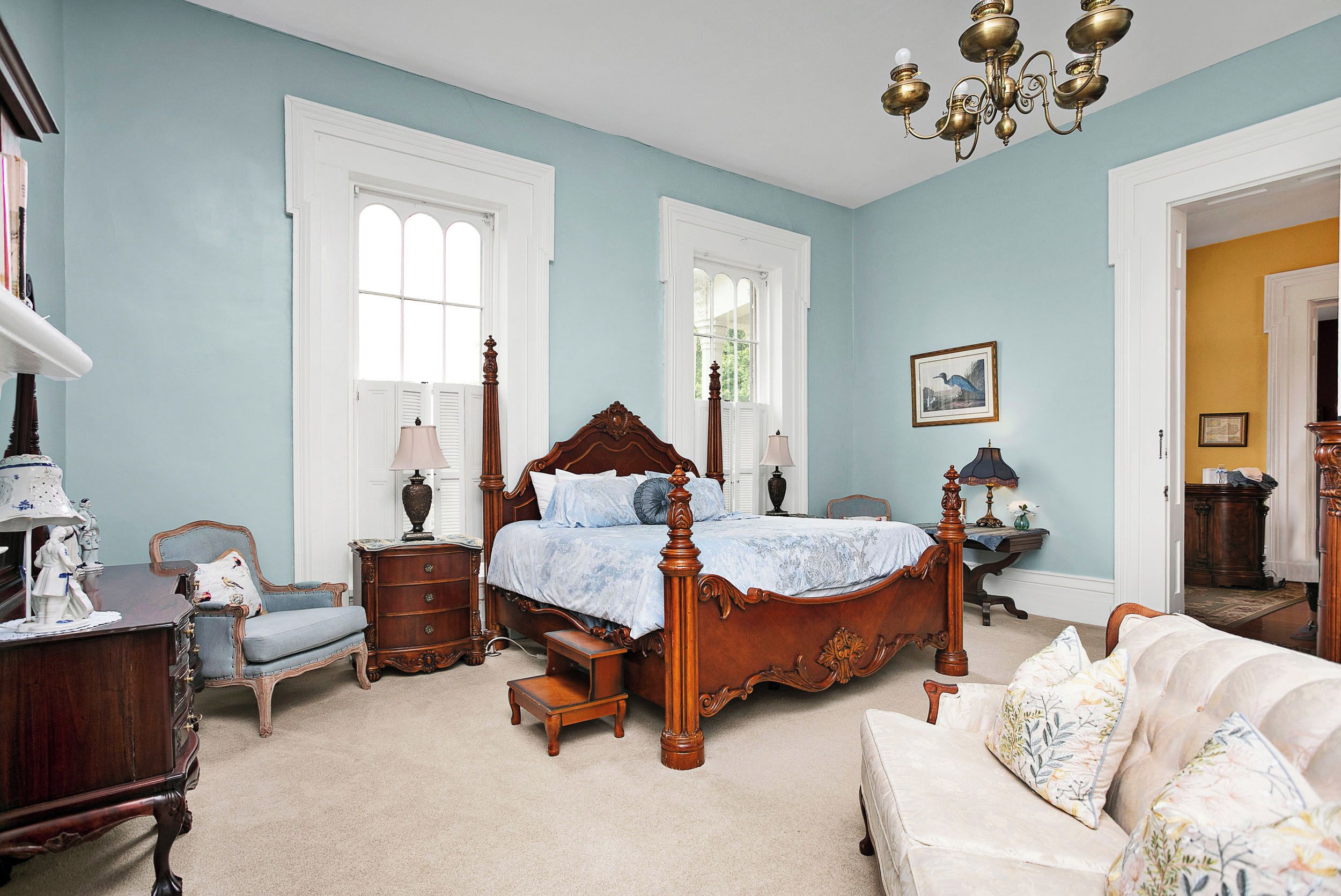 Um quarto com cama de dossel, uma cadeira, cômoda e sofá.