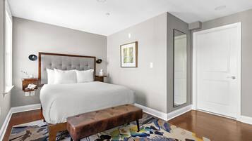 Quarto com cama, banqueta, mesa de cabeceira e porta.