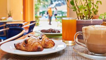 Disposição para o pequeno-almoço com croissants, um copo de sumo de laranja e uma chávena de café sobre uma mesa.