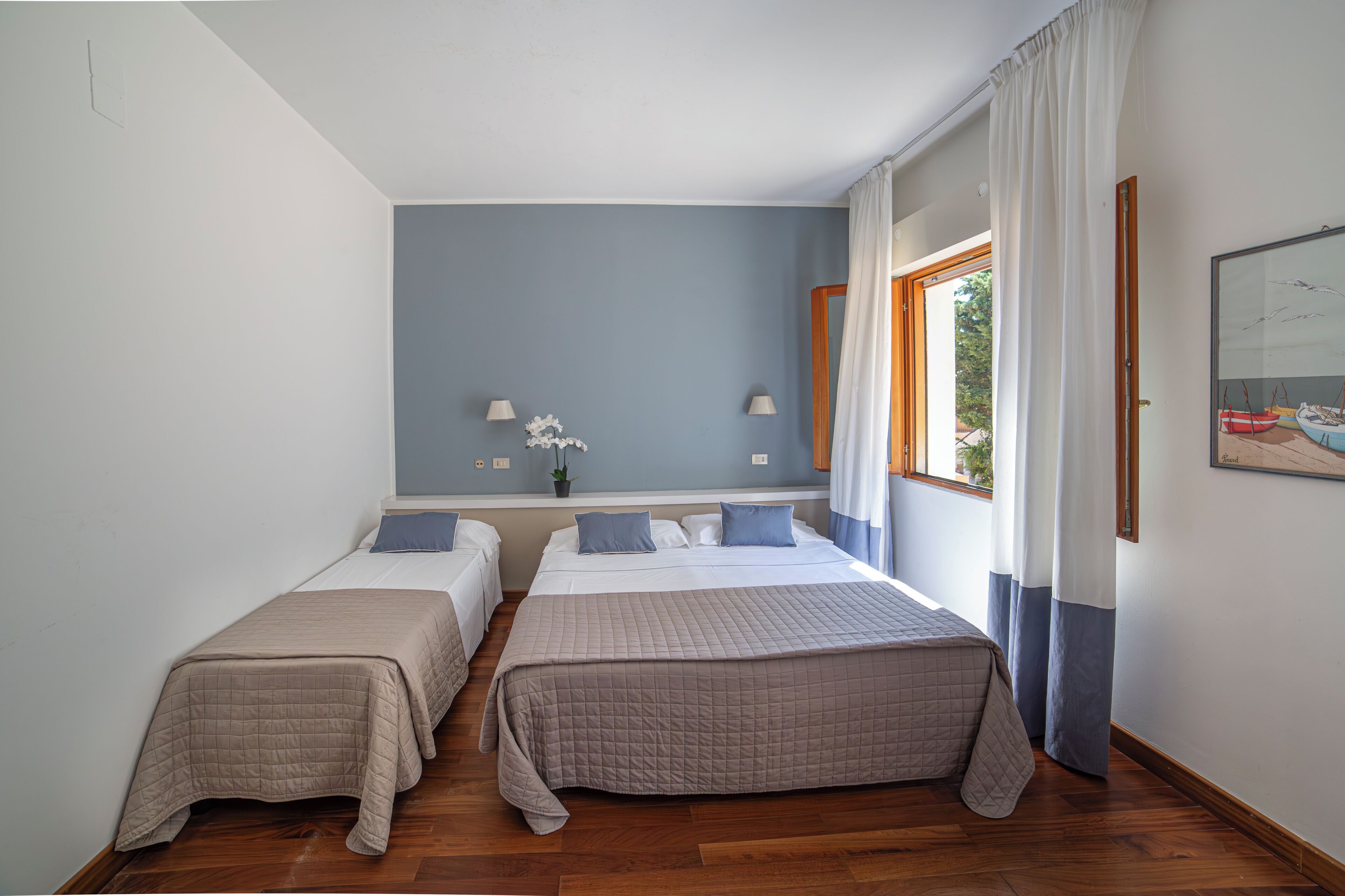 Quarto com duas camas, uma janela com cortinas, uma planta e um quadro na parede.