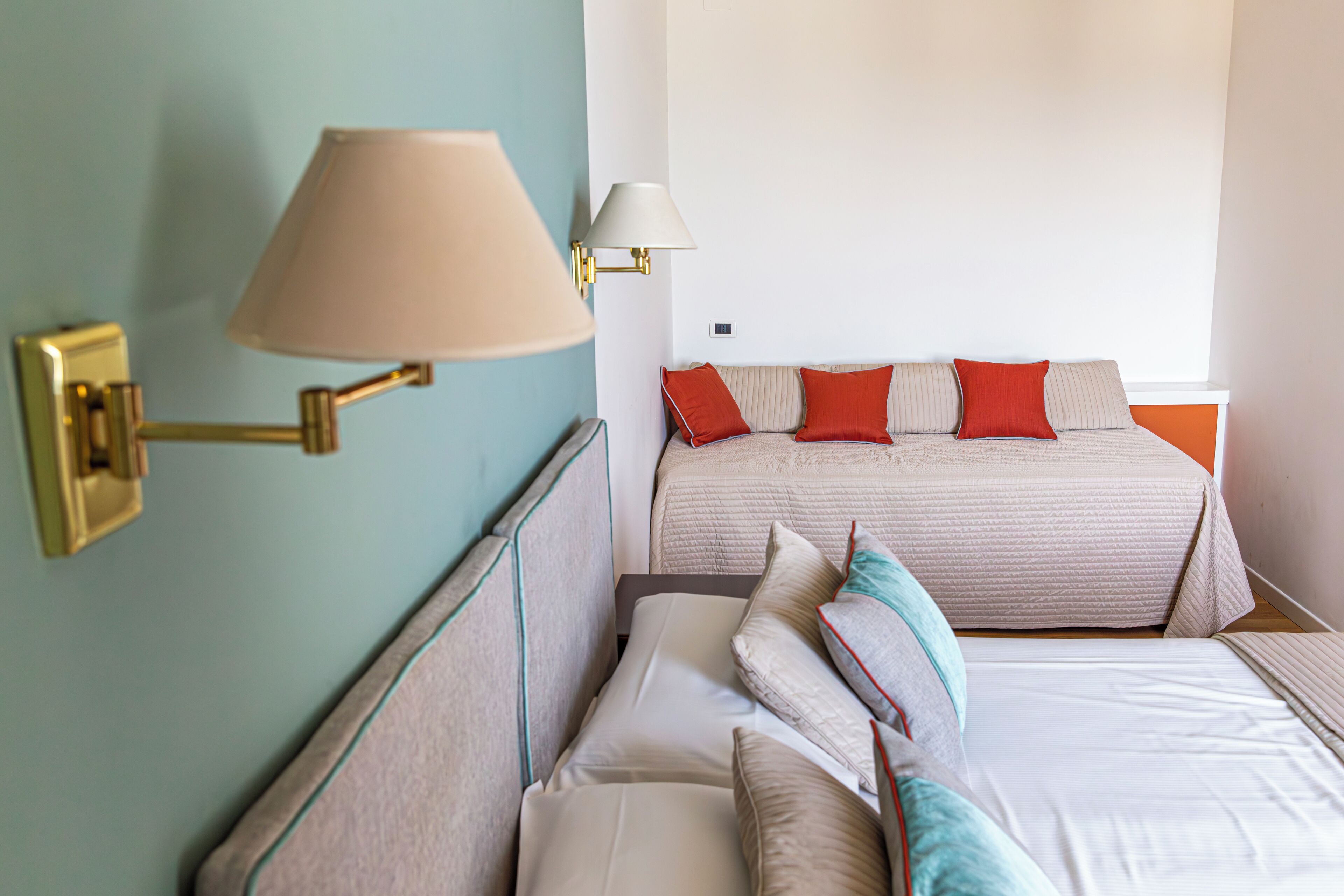 Quarto de hotel com duas camas, uma luminária fixada na parede e uma janela com persianas.