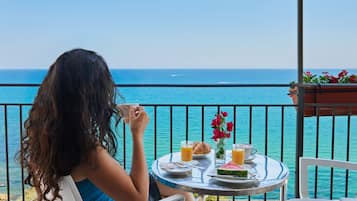 Pessoa sentada à mesa com vista para o mar, um prato de comida e um copo de suco de laranja.