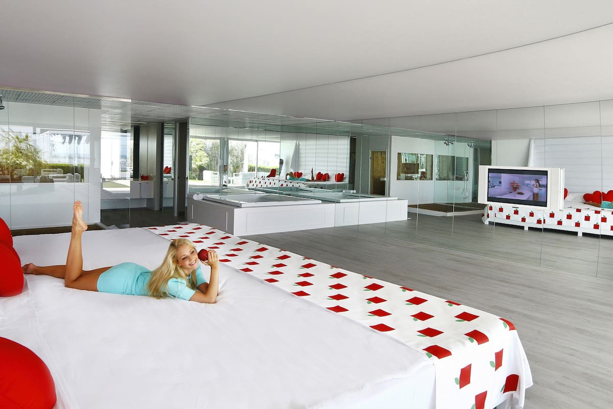 Quarto de hotel moderno com uma cama grande, televisão e vista para o exterior.