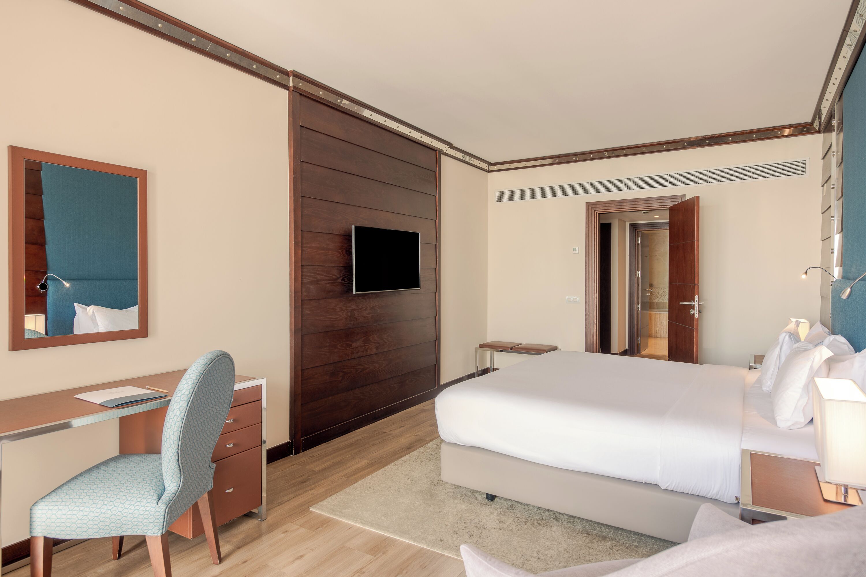 Quarto de hotel com cama, escrivaninha, cadeira e televisão.
