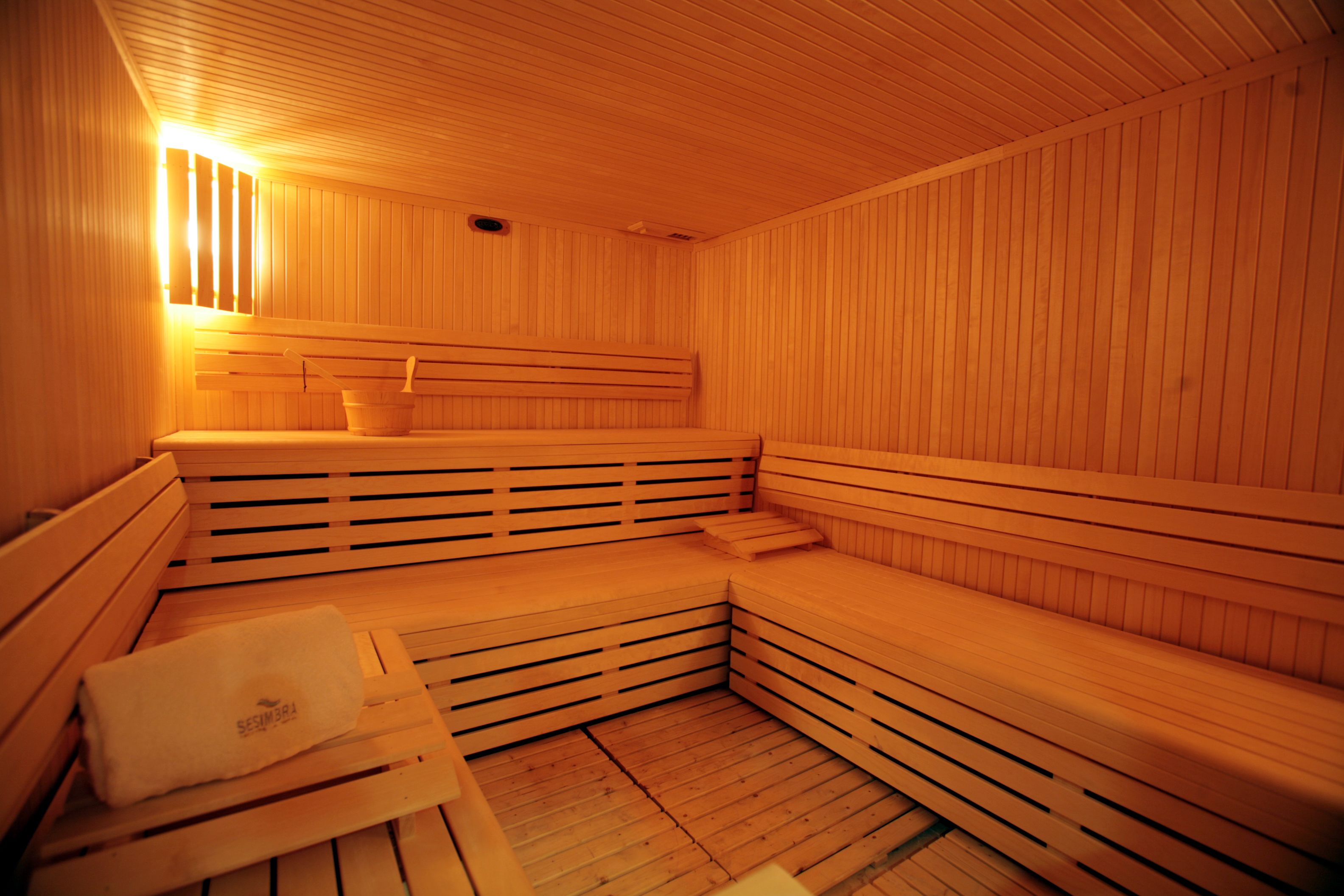 Uma sauna com bancos de madeira, um banco com toalha e aquecedor na parede.