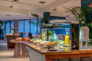 Uma área de buffet com diversos tipos de comida, uma máquina de café e uma escultura decorativa em tom de azul-turquesa.