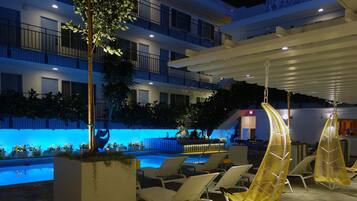 Uma área de piscina em hotel com espreguiçadeiras e um espaço coberto para relaxar.