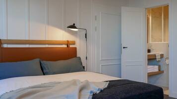 Uma cama bem arrumada com cabeceira de madeira, luminária de cabeceira e prateleira com toalhas e produtos de higiene pessoal.