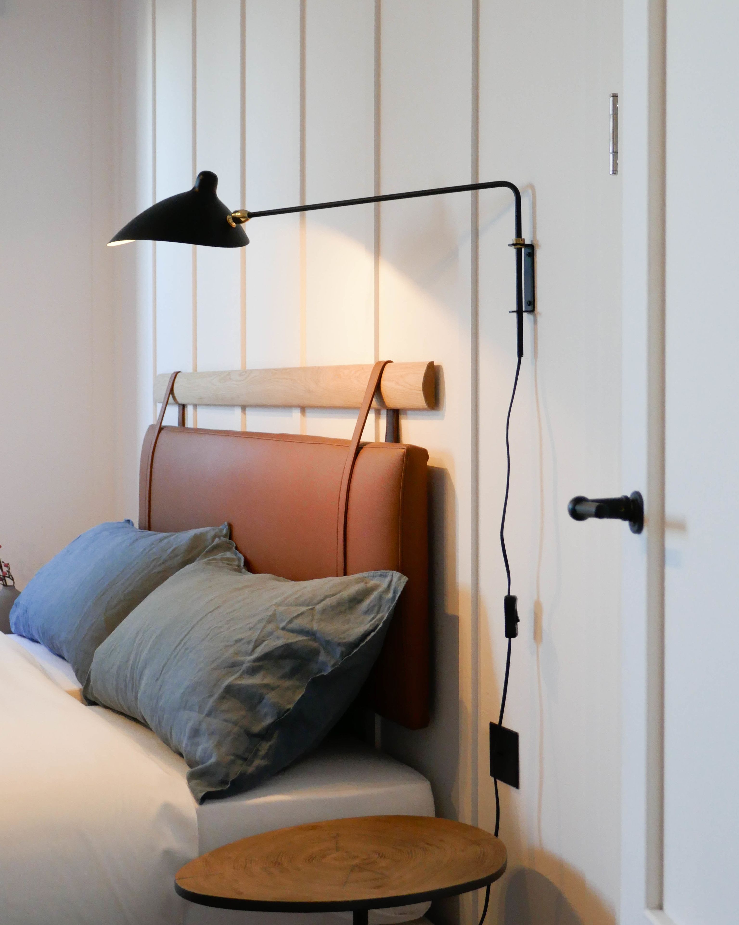 Quarto com cama, almofadas, mesa de cabeceira, abajur e porta.