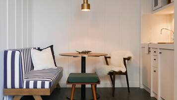 Um espaço de estar compacto com um sofá listrado, uma pequena mesa redonda, uma poltrona com um cobertor de pele e uma área de cozinha com armários e micro-ondas.