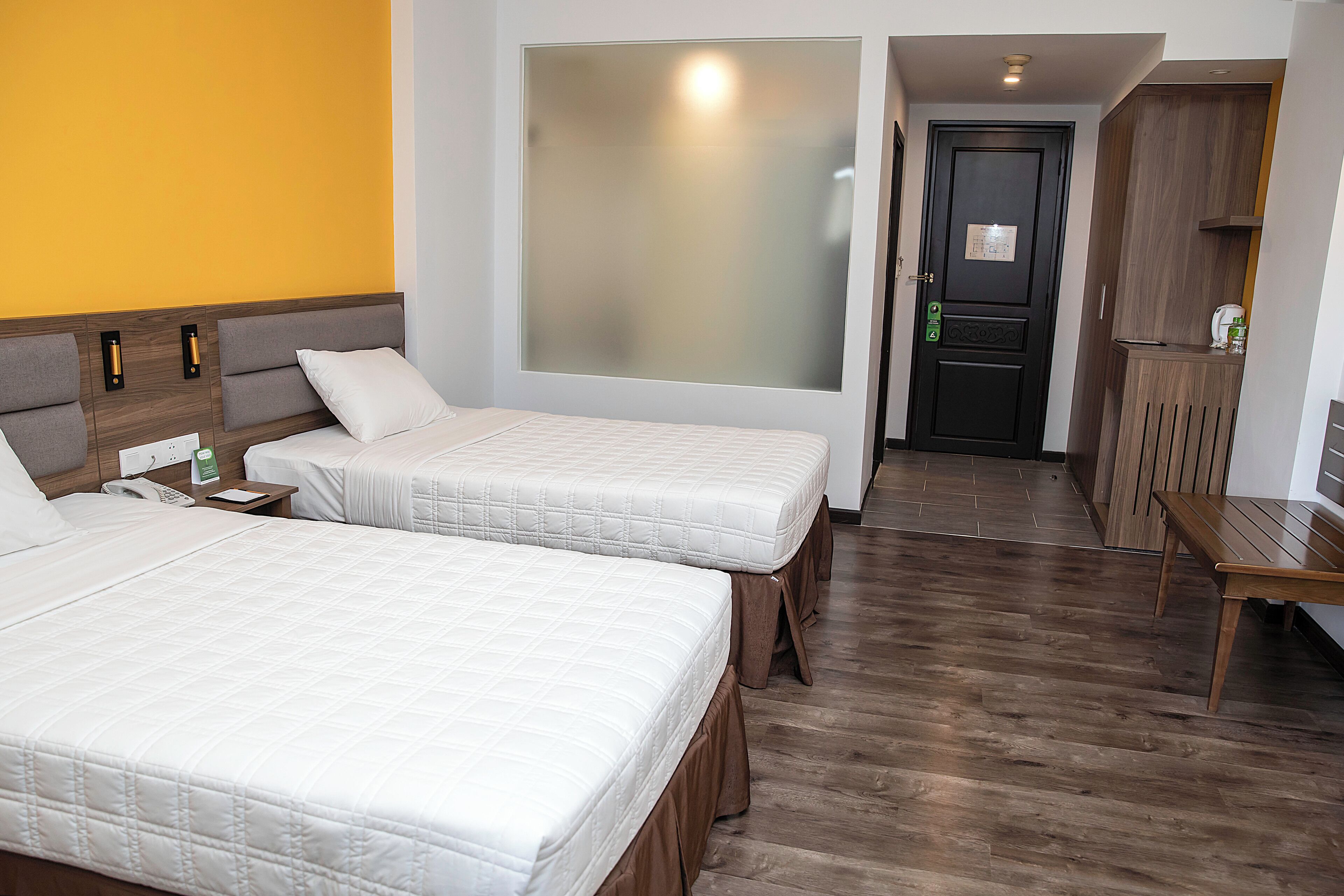 Quarto de hotel com duas camas, piso de madeira, um guarda-roupa e uma mesinha.