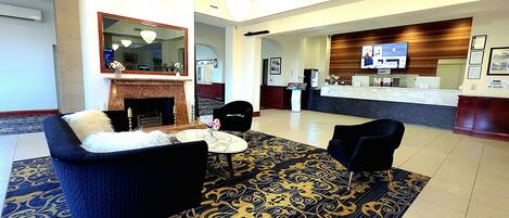 Um hall de hotel com balcão de recepção, lareira, área de estar e um tapete grande com padrão.