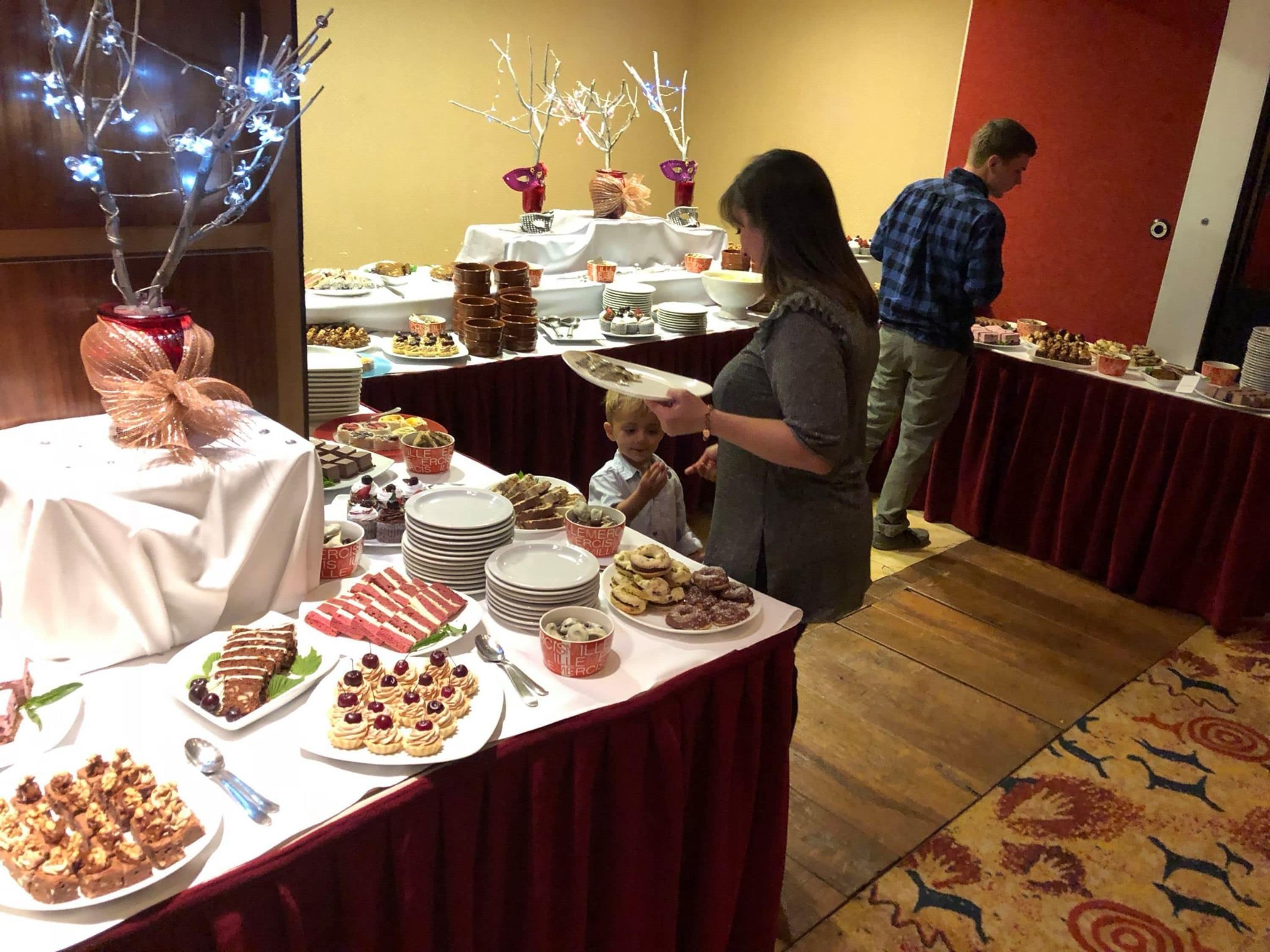 Uma mesa de buffet com diversos doces e uma pessoa servindo comida.