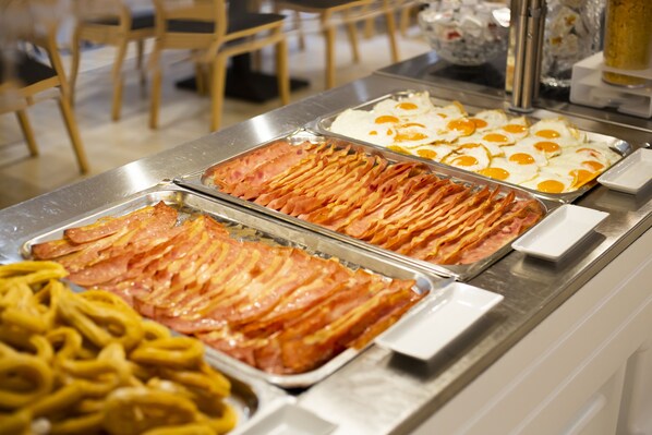 Buffet com diversas opções de comida, incluindo bacon, ovos e massa.