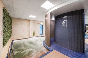 Uma área de spa com hidromassagem, parede com jardim vertical e parede revestida de azulejos azuis com o símbolo de um chuveiro.