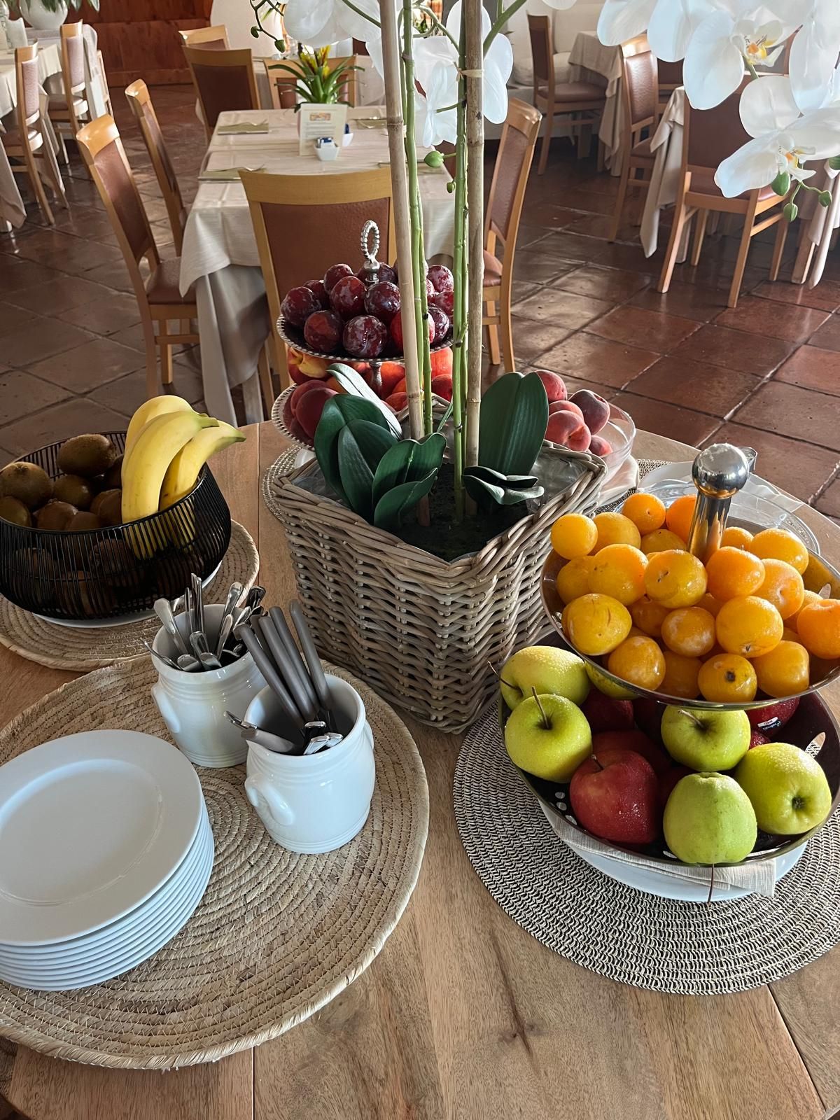 Uma mesa posta com frutas, uma planta em vaso e um objeto decorativo.