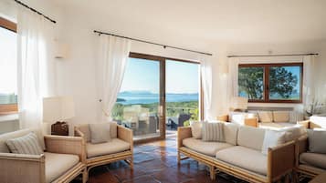 Uma sala de estar espaçosa com uma grande janela que oferece uma vista panorâmica, móveis de vime e piso de azulejos.