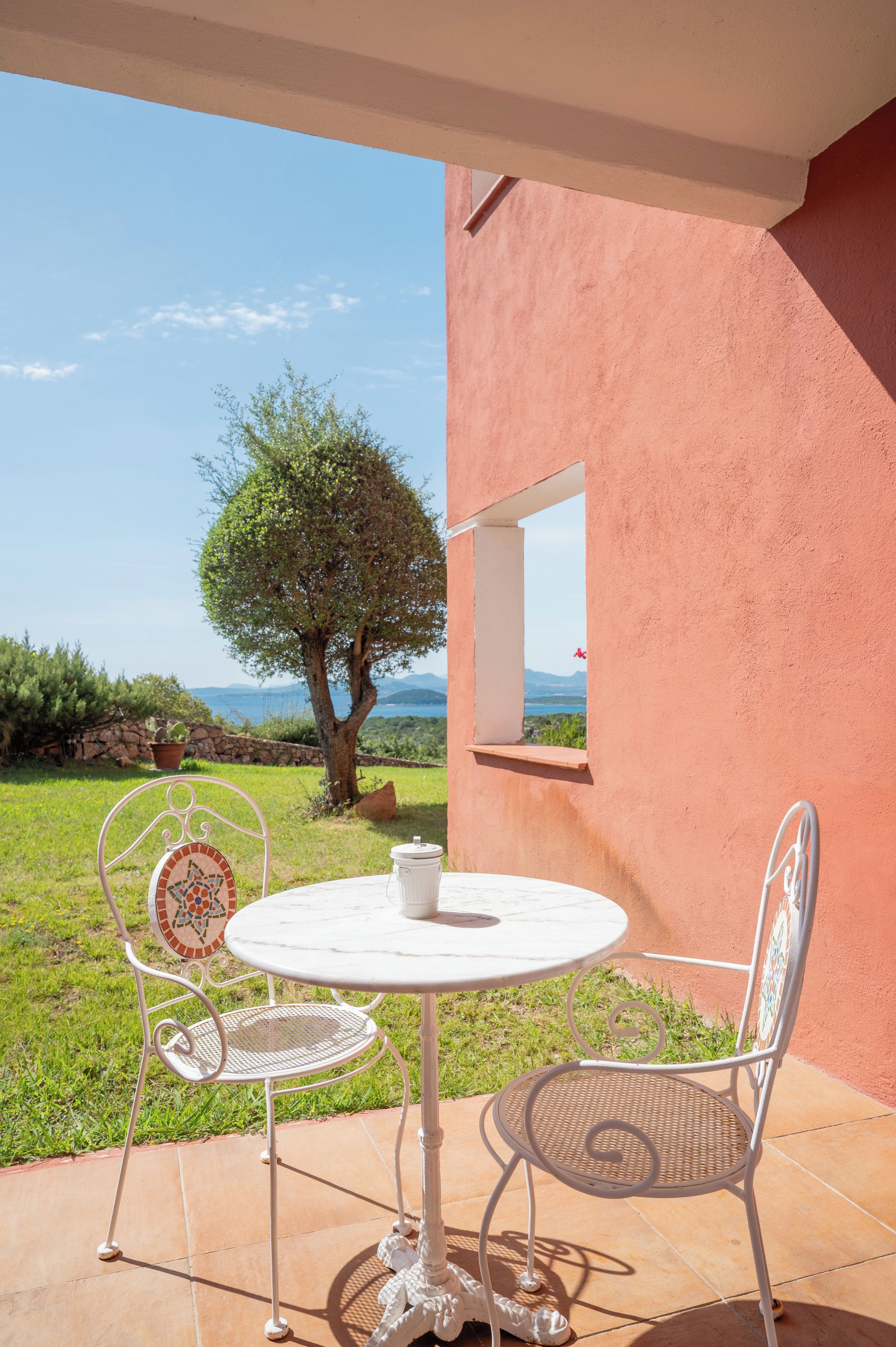 Um pátio com mesa e cadeiras, vista para uma árvore e um edifício com parede rosa.