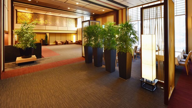 Um hall amplo com teto alto, diversas áreas de estar e grandes vasos de plantas.