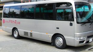 Um ônibus prateado estacionado no acostamento de uma estrada, com um edifício ao fundo.