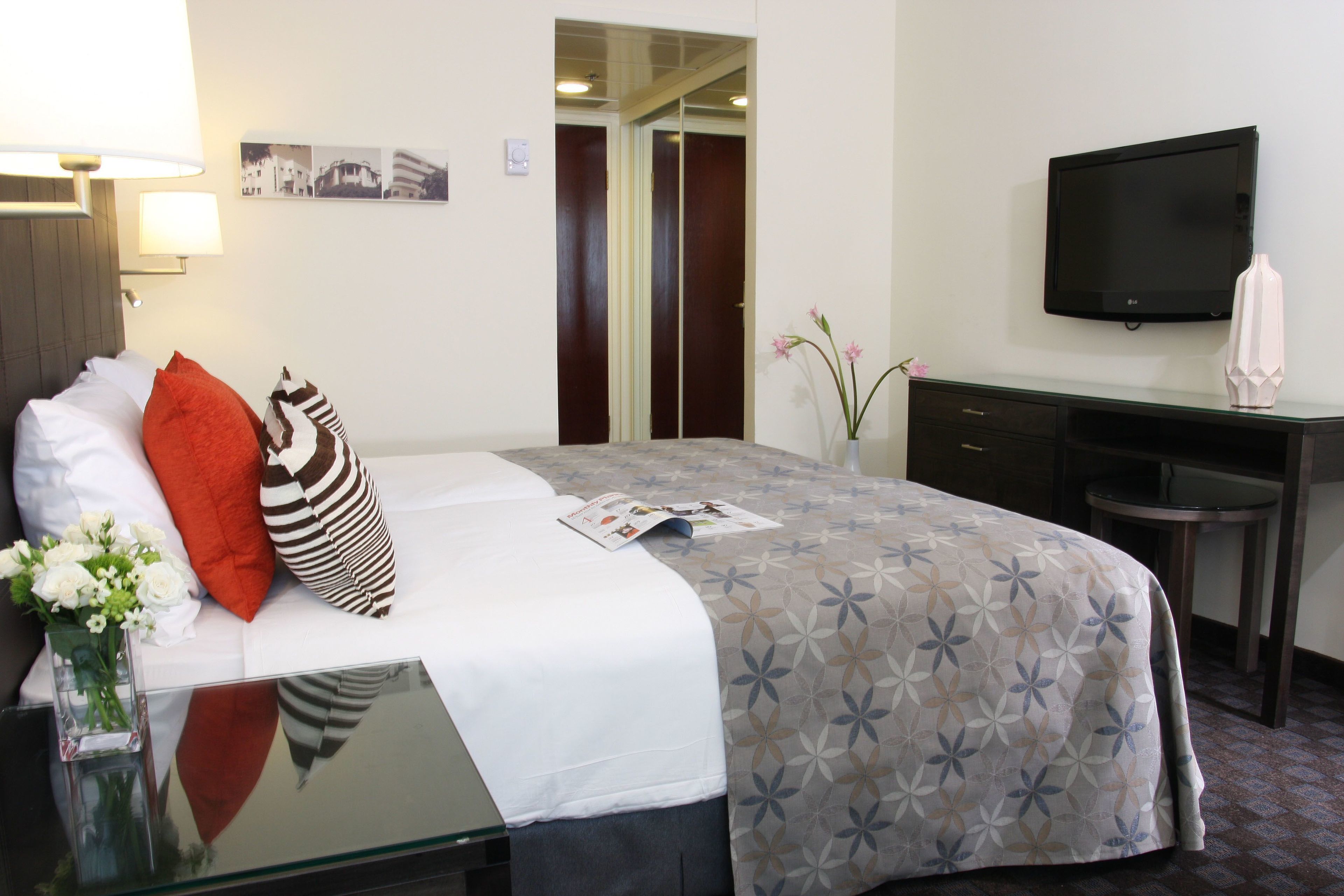 Quarto de hotel com uma cama, uma escrivaninha, uma televisão e um espelho.