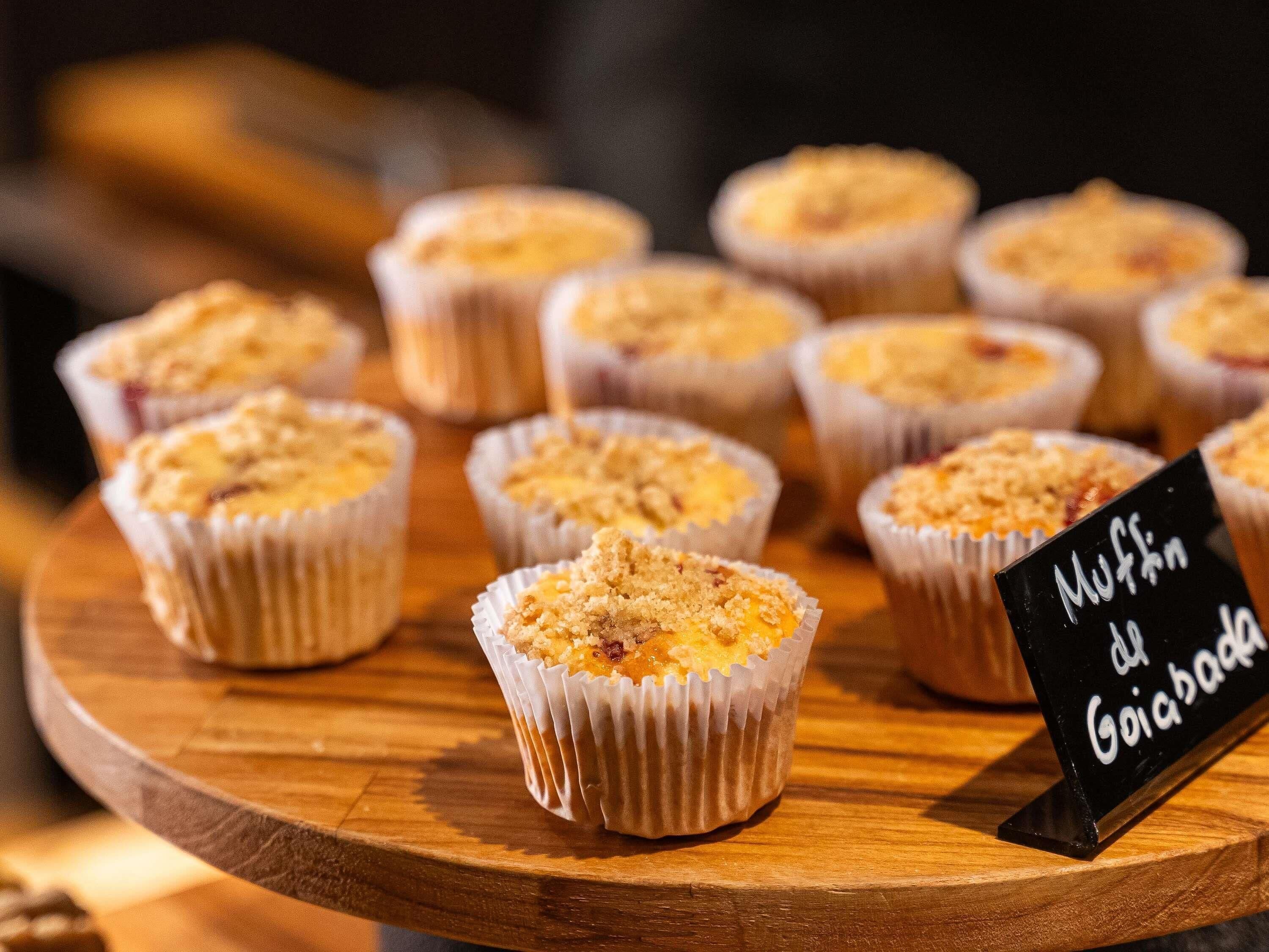 Uma mesa de madeira com forminhas de muffin dispostas sobre ela, e um letreiro com a inscrição 'Muffin de Goa'.