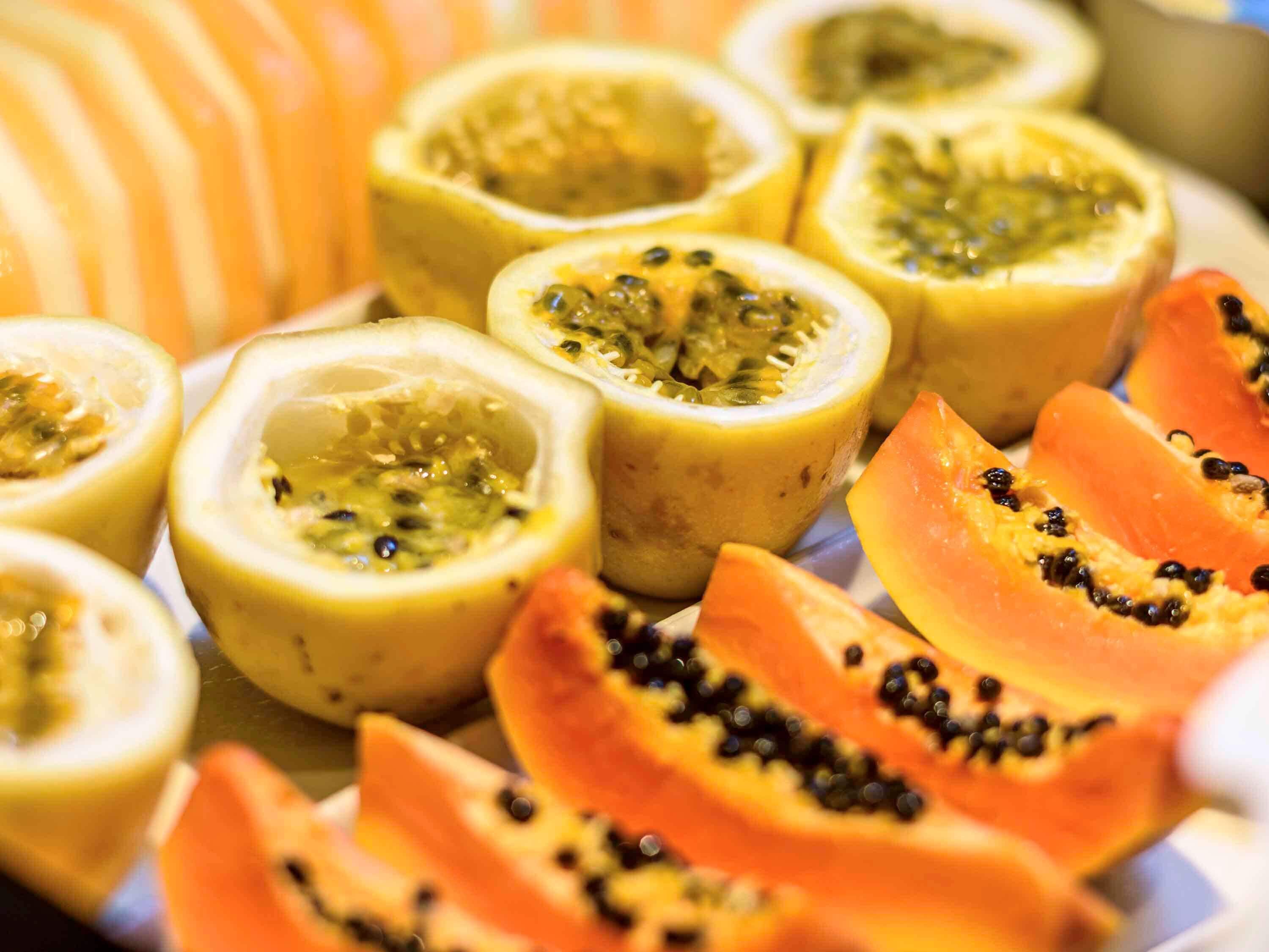 Diversas frutas fatiadas, incluindo mamão e maracujá.