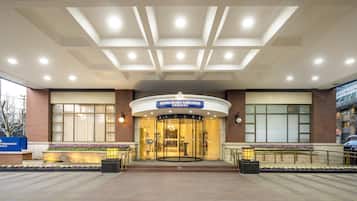 Entrada de hotel com porta giratória de vidro, um sinal azul acima da porta e fachada de tijolos.