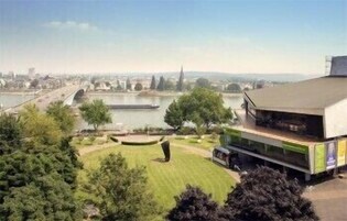 Um edifício moderno com telhado plano e amplas janelas com vista para um rio e paisagem urbana.
