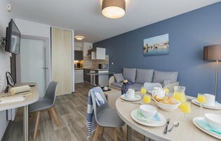 Uma sala de estar moderna com um sofá, mesa de jantar posta para o café da manhã e uma cozinha ao fundo.