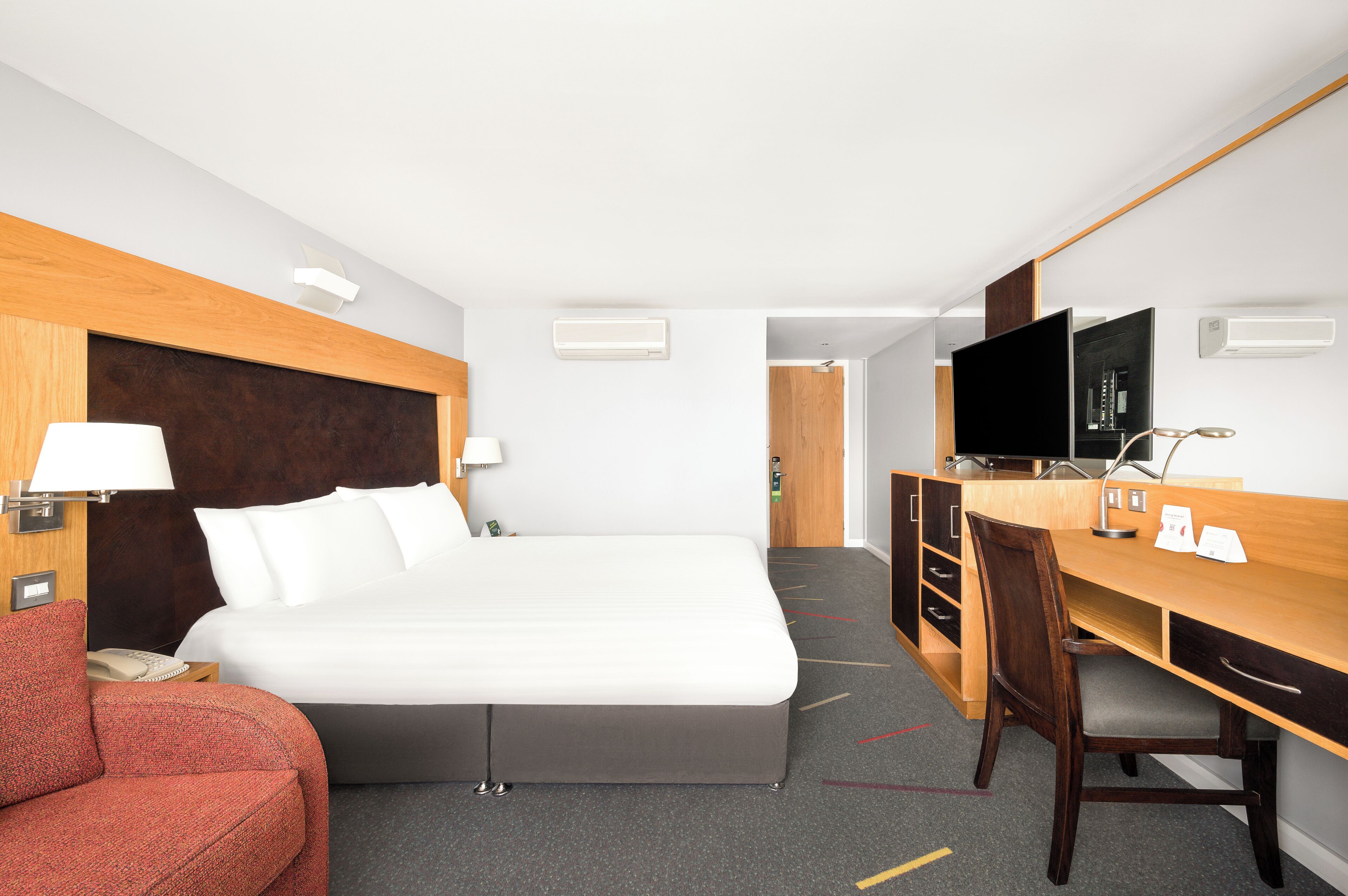 Quarto de hotel com cama, escrivaninha, cadeira e televisão.