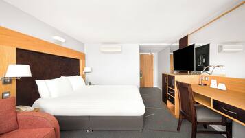 Quarto de hotel com cama, escrivaninha, cadeira e televisão.