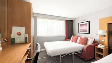 Quarto de hotel com cama, escrivaninha, cadeira, mesa de cabeceira com abajur, quadro na parede e janela com cortinas.
