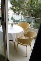 Uma varanda com uma mesa e duas cadeiras de vime, com vista para uma árvore e um edifício.