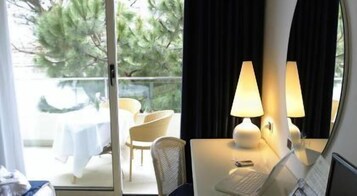 Quarto de hotel com varanda, mesa, duas cadeiras e um abajur.