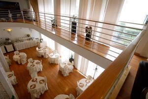 Quarto de hotel em vários níveis, com mesas e cadeiras redondas, uma varanda com plantas em vasos e uma escadaria.