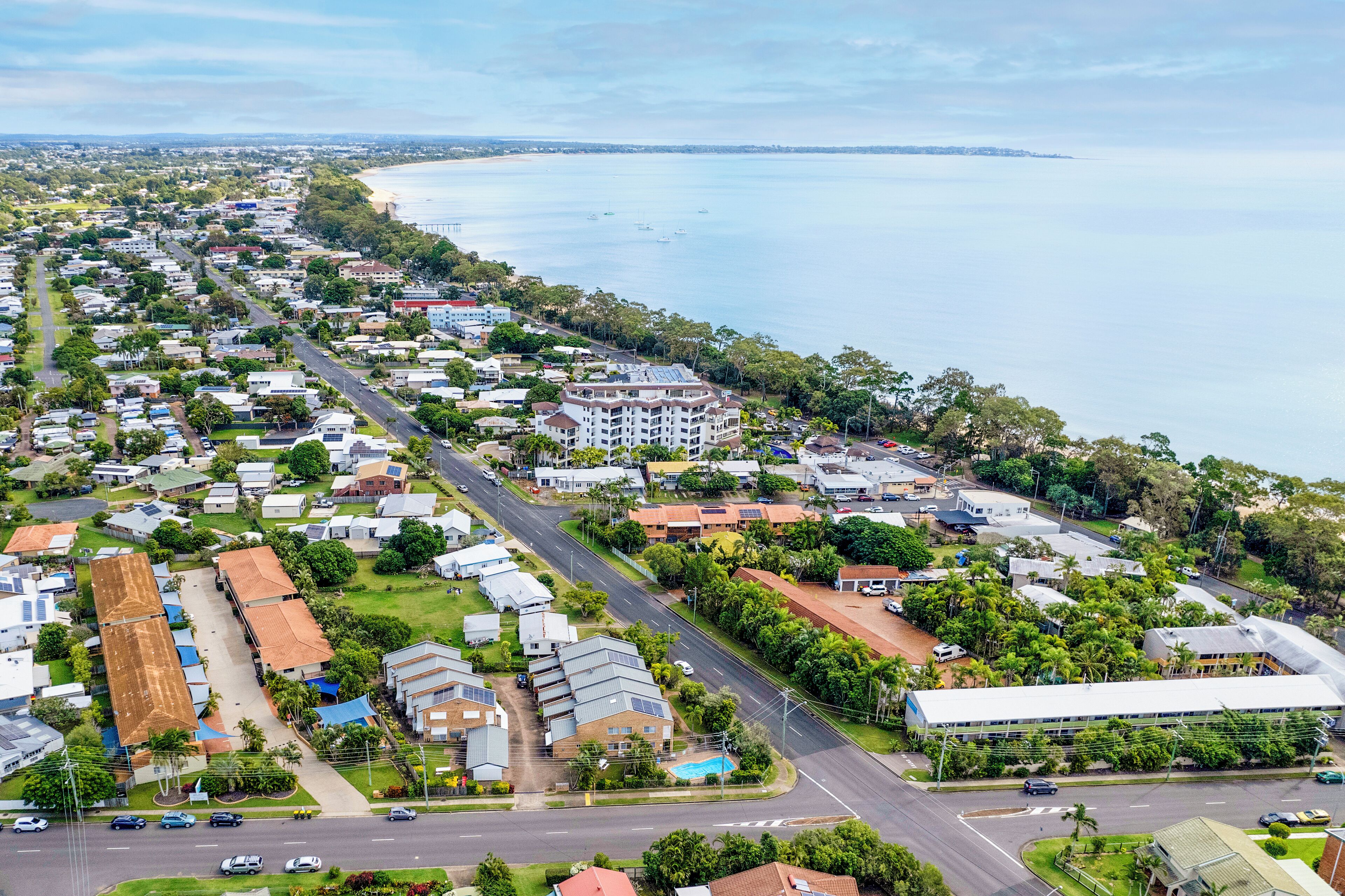 Vista aérea de uma área residencial costeira com casas, uma avenida principal e uma praia ao fundo.