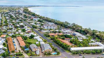Vista aérea de uma área residencial costeira com casas, uma avenida principal e uma praia ao fundo.