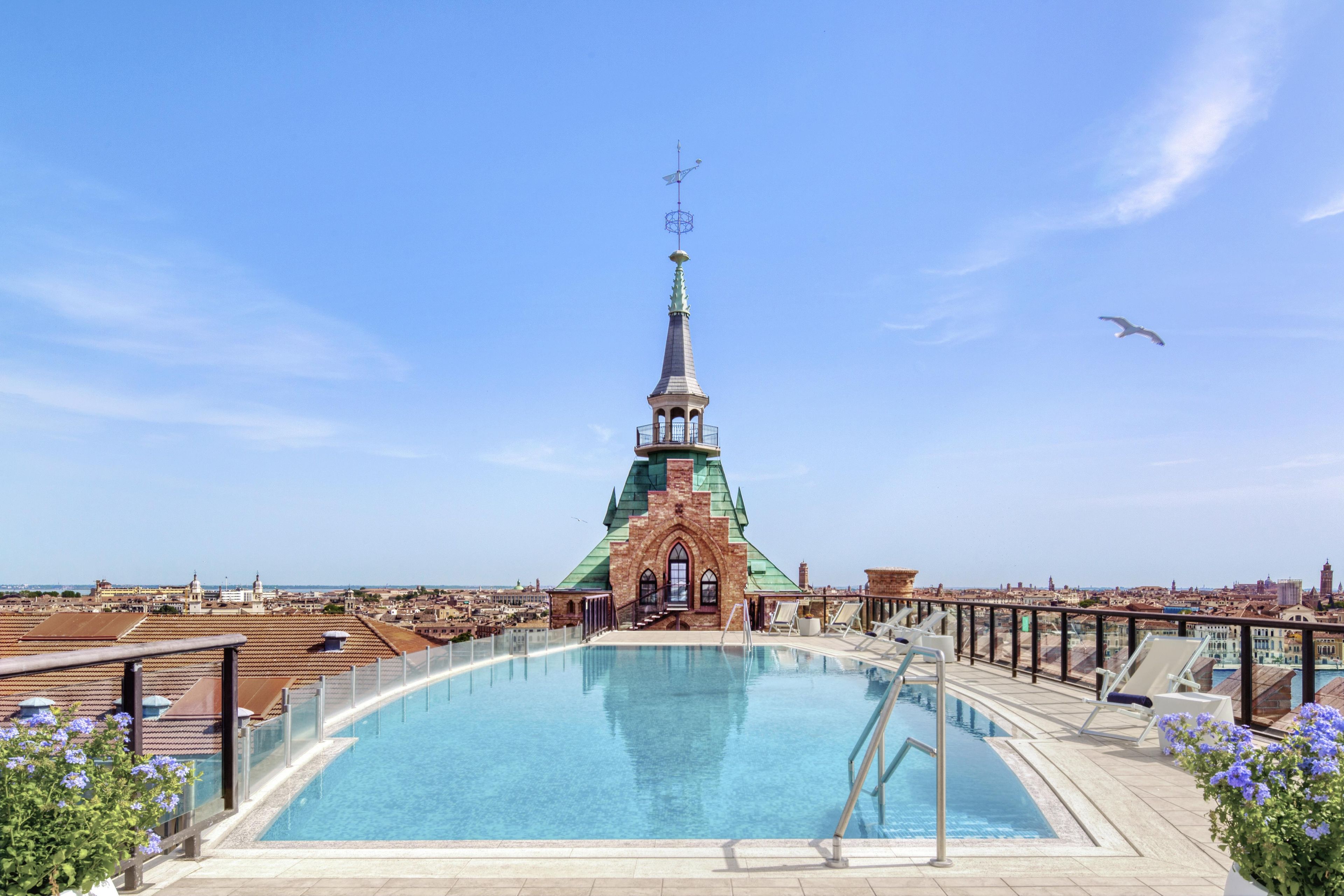 Piscina no terraço com vista para um edifício histórico com telhado verde e torre.