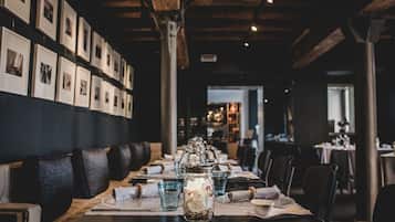 Um restaurante com uma mesa comprida posta para refeições, quadros nas paredes e teto de madeira rústica.