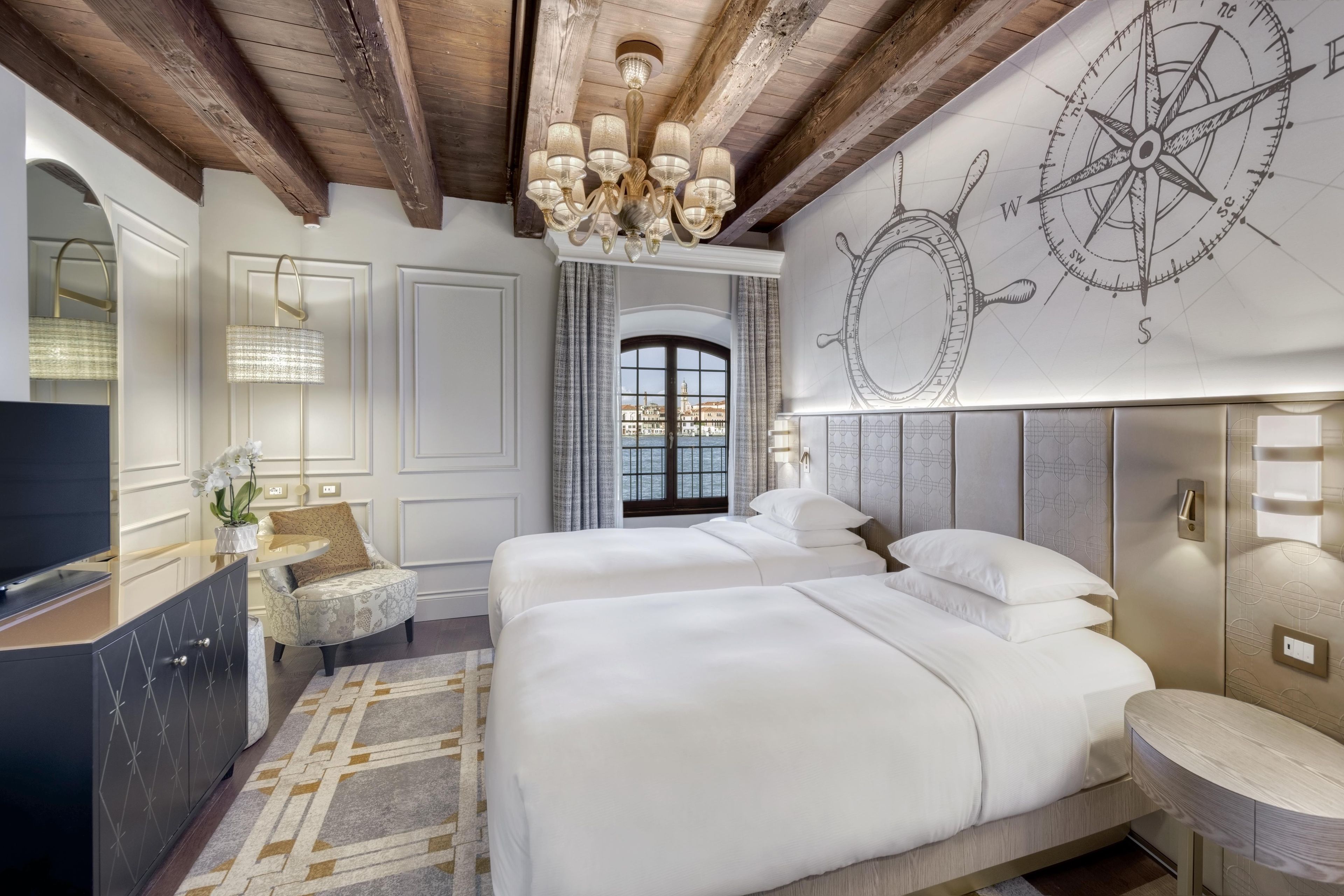 Quarto de hotel com cama grande, escrivaninha, lustre e mapa na parede.