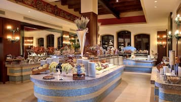 Lobby de hotel com ilha central exibindo um buffet, rodeado por áreas de estar e teto decorativo.